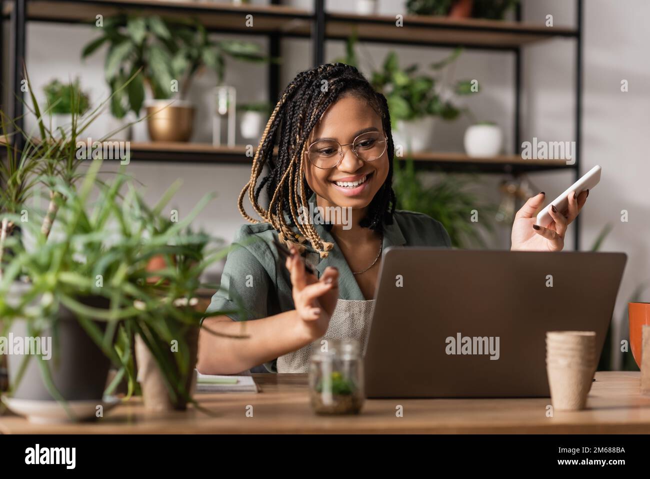 happy african american florist holding smartphone and gesturing during ...