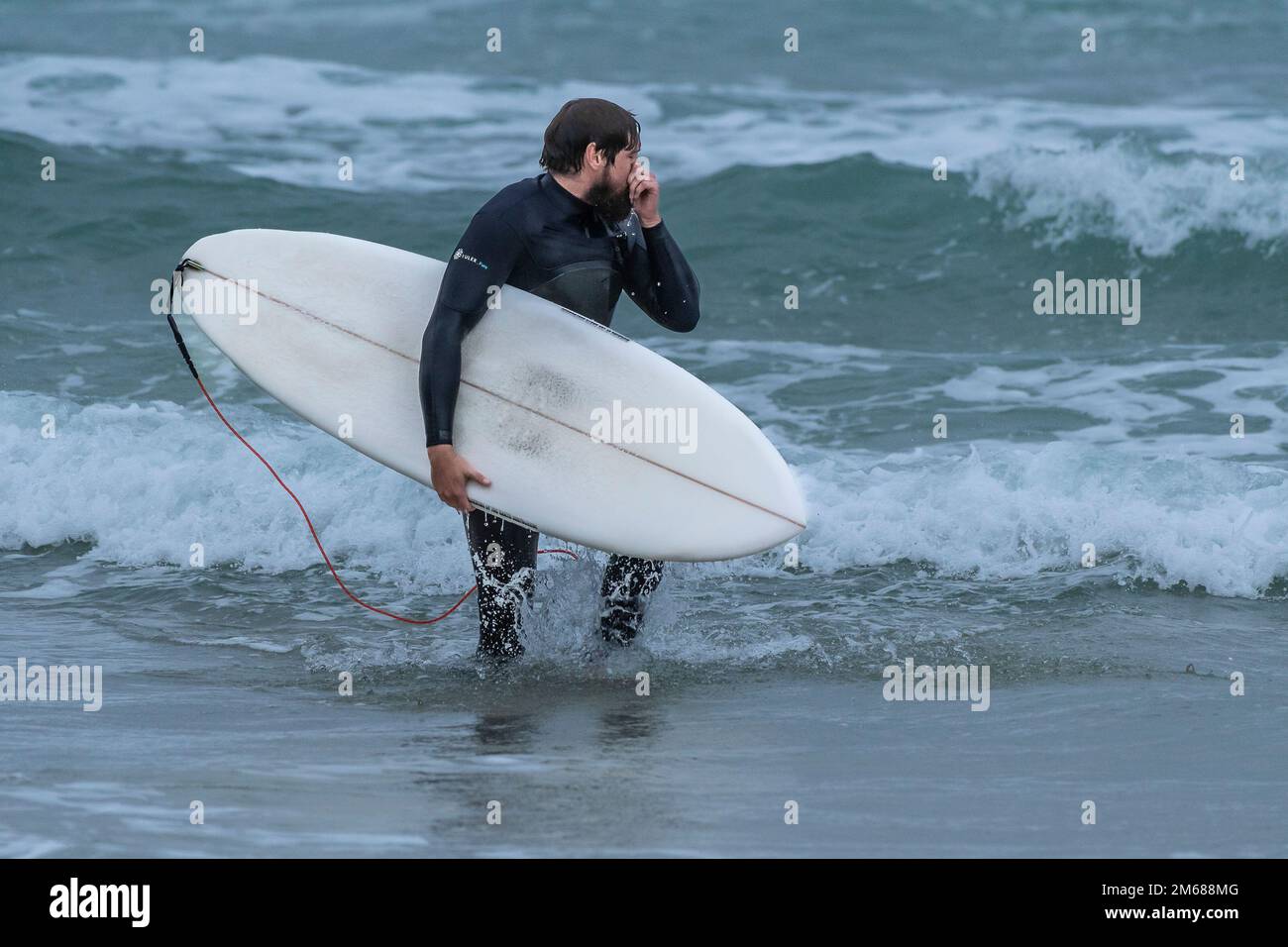 A tired surfer carrying his surfboard walking out of the sea at Fistral ...