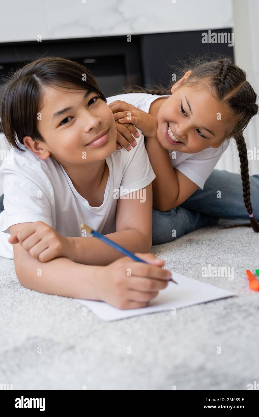 Smiling asian girl looking at brother drawing on paper at home,stock ...