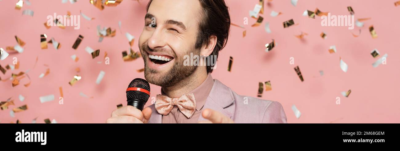 Stylish host of event holding microphone and winking at camera under ...