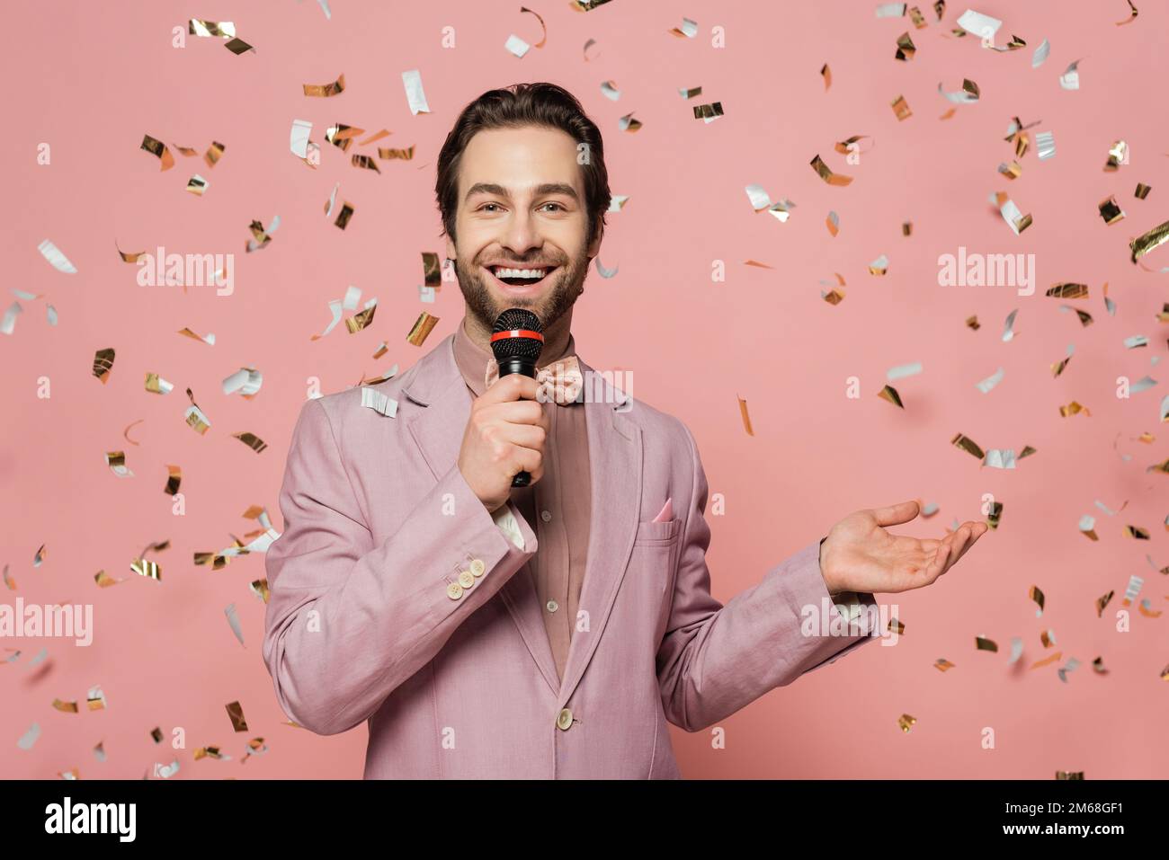 Positive host of event holding microphone under falling confetti on ...