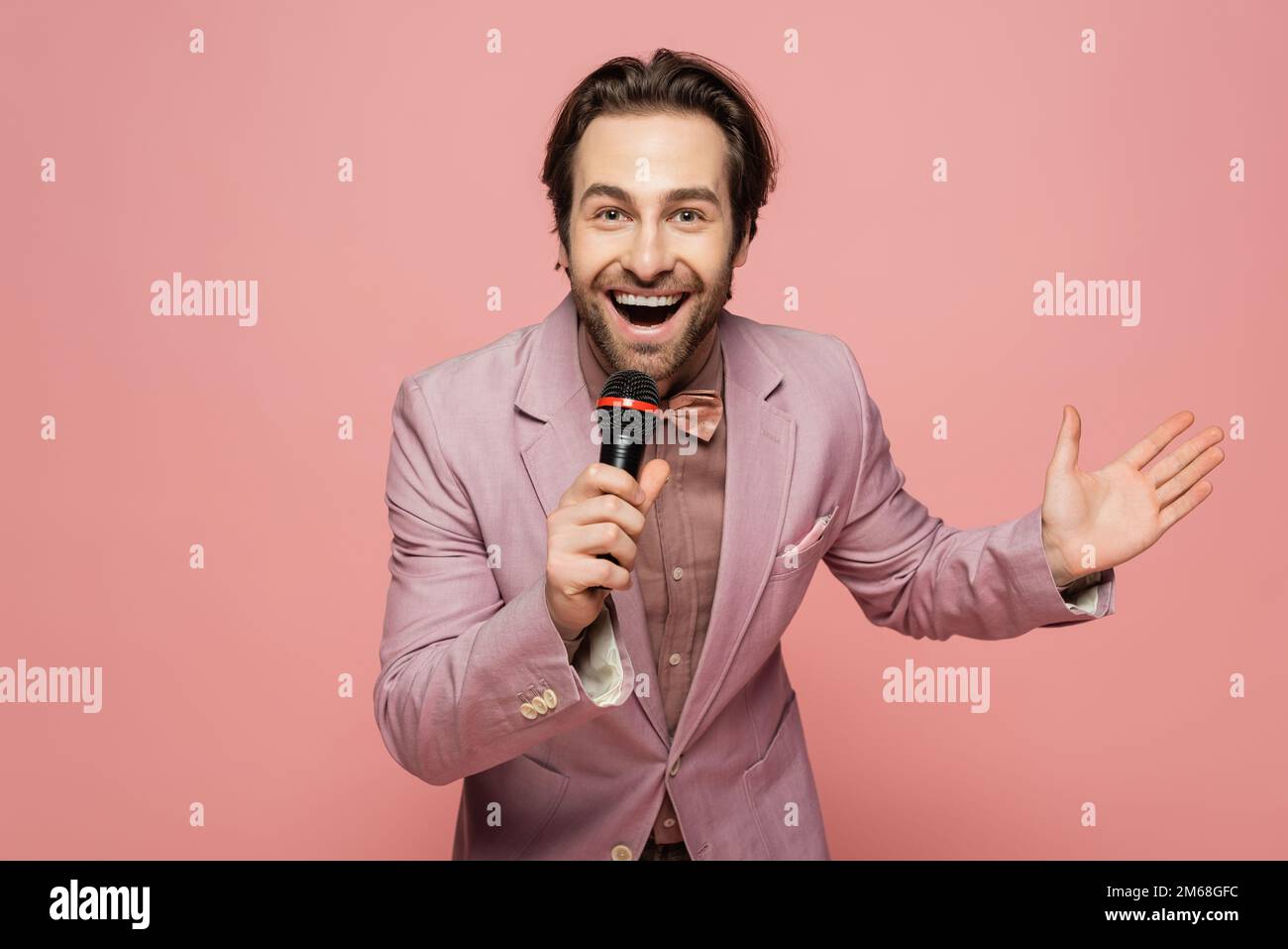 Cheerful host of event talking at microphone and waving hand isolated ...