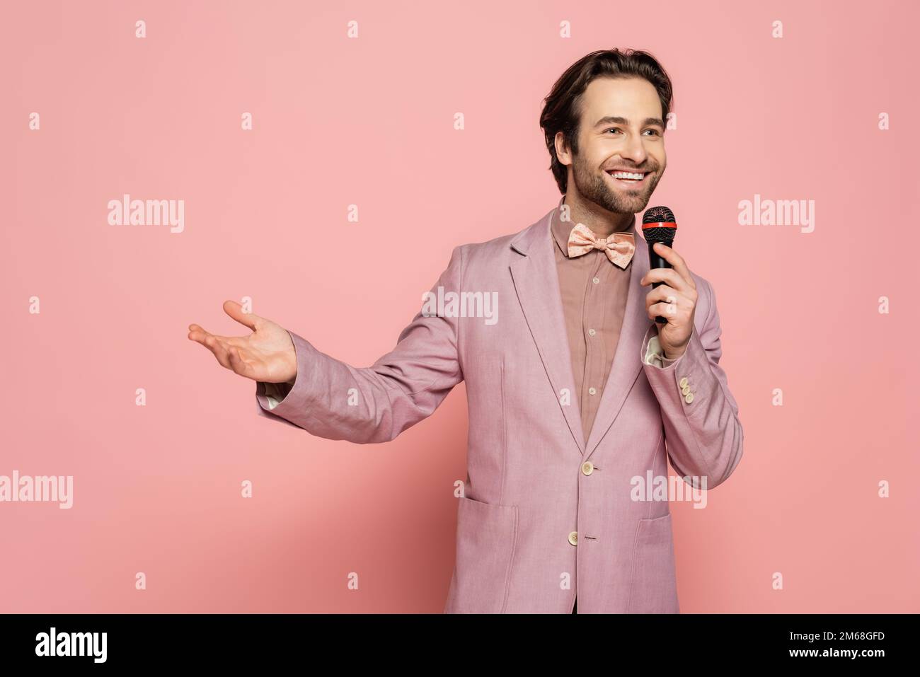 Positive host of event talking and holding microphone on pink ...