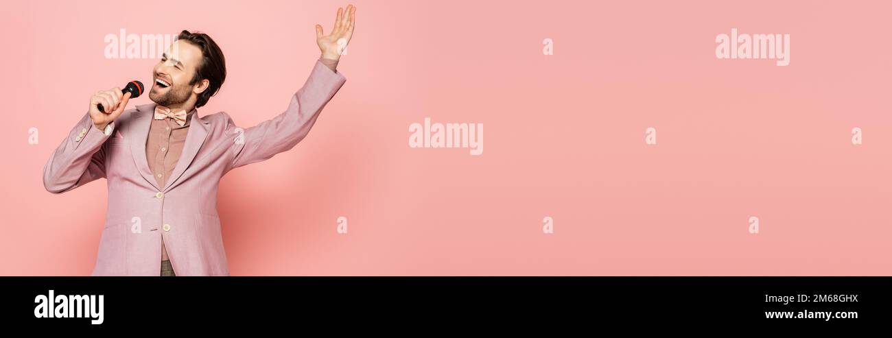 Stylish host of event singing at microphone on pink background, banner ...