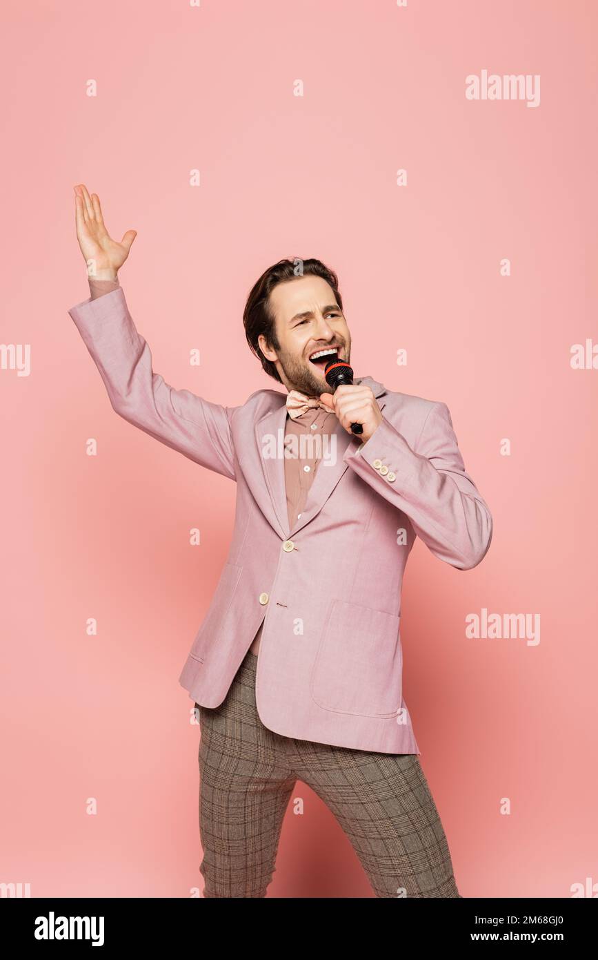 Cheerful host of event singing while holding microphone on pink ...