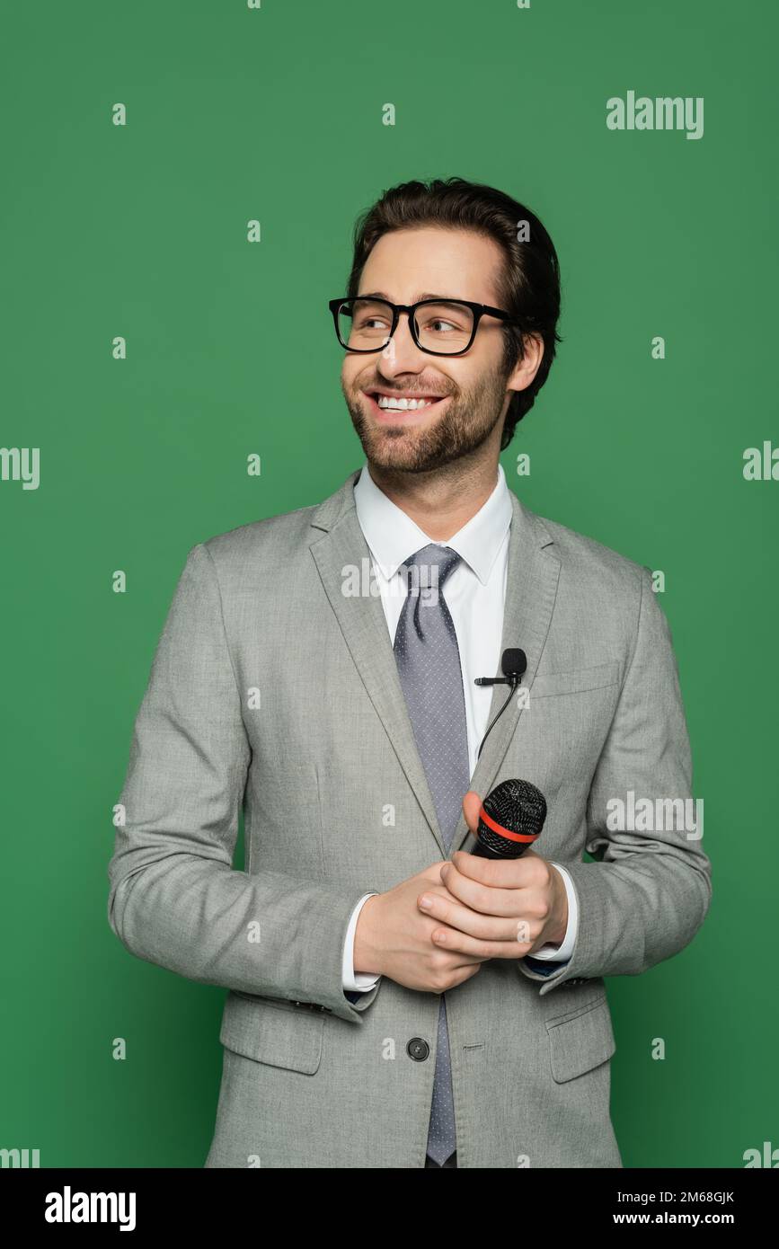 happy news anchor in suit and eyeglasses holding microphone isolated on ...