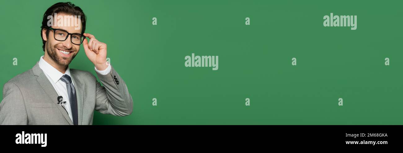 news anchor in suit adjusting eyeglasses while smiling on green ...