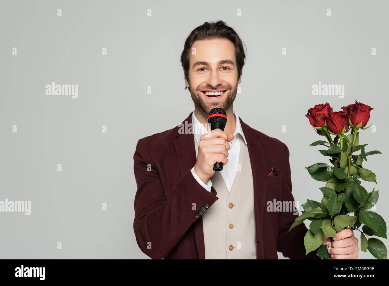 cheerful host of event in blazer holding red roses and talking in ...