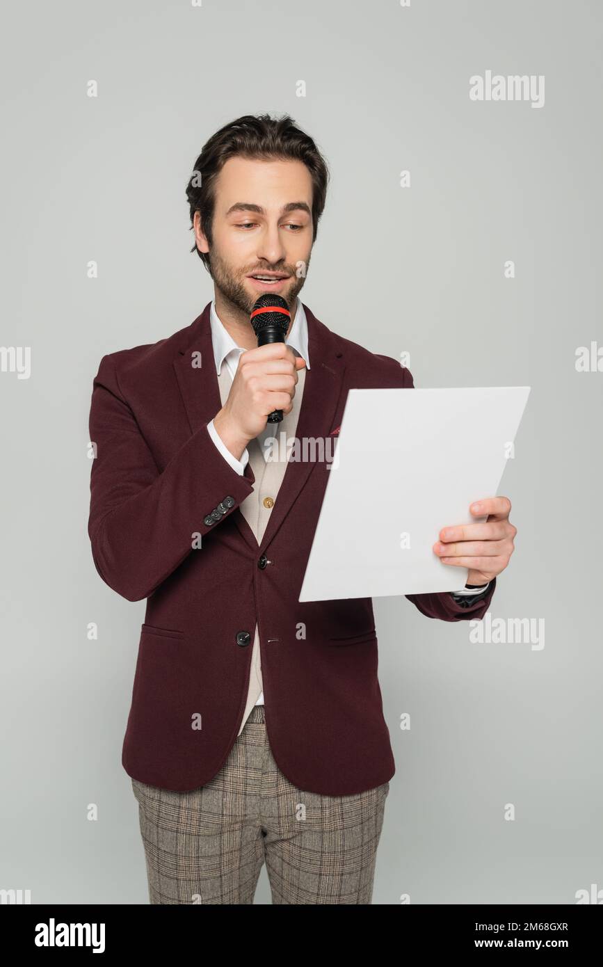 bearded host of event in formal wear making announcement in microphone ...