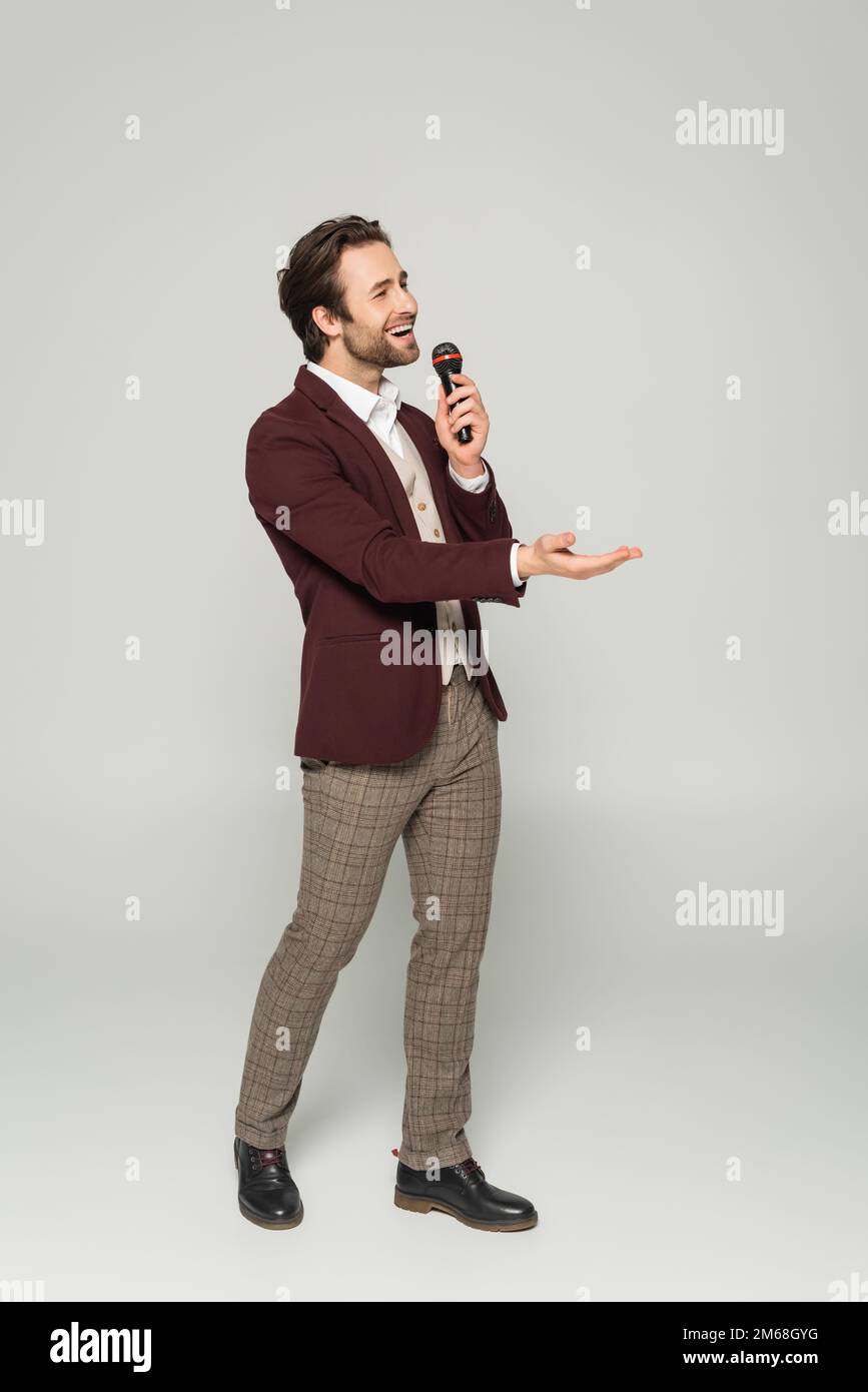 full length of bearded showman in formal wear singing in microphone on ...