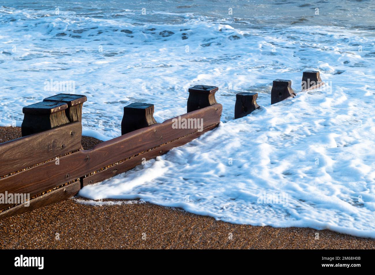 A beach groyne on the beach at Bexhill-on-Sea with waves and foam ...