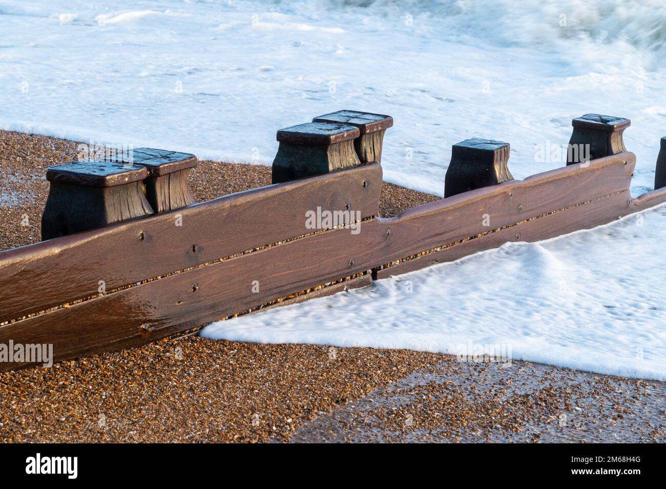 A beach groyne on the beach at Bexhill-on-Sea with waves and foam ...
