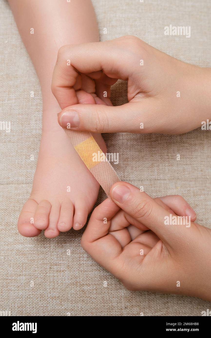 Mother woman sticks a medical band-aid on the toddler baby leg. Mom s ...