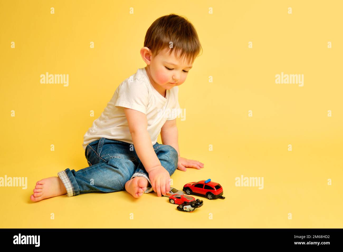 Toddler baby plays with toy cars on a studio yellow background. Happy ...