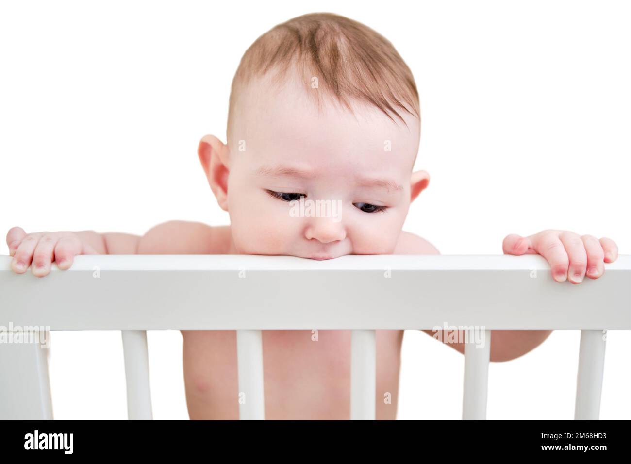 Baby gnaws at the edge crib during teething itching, isolated on a ...