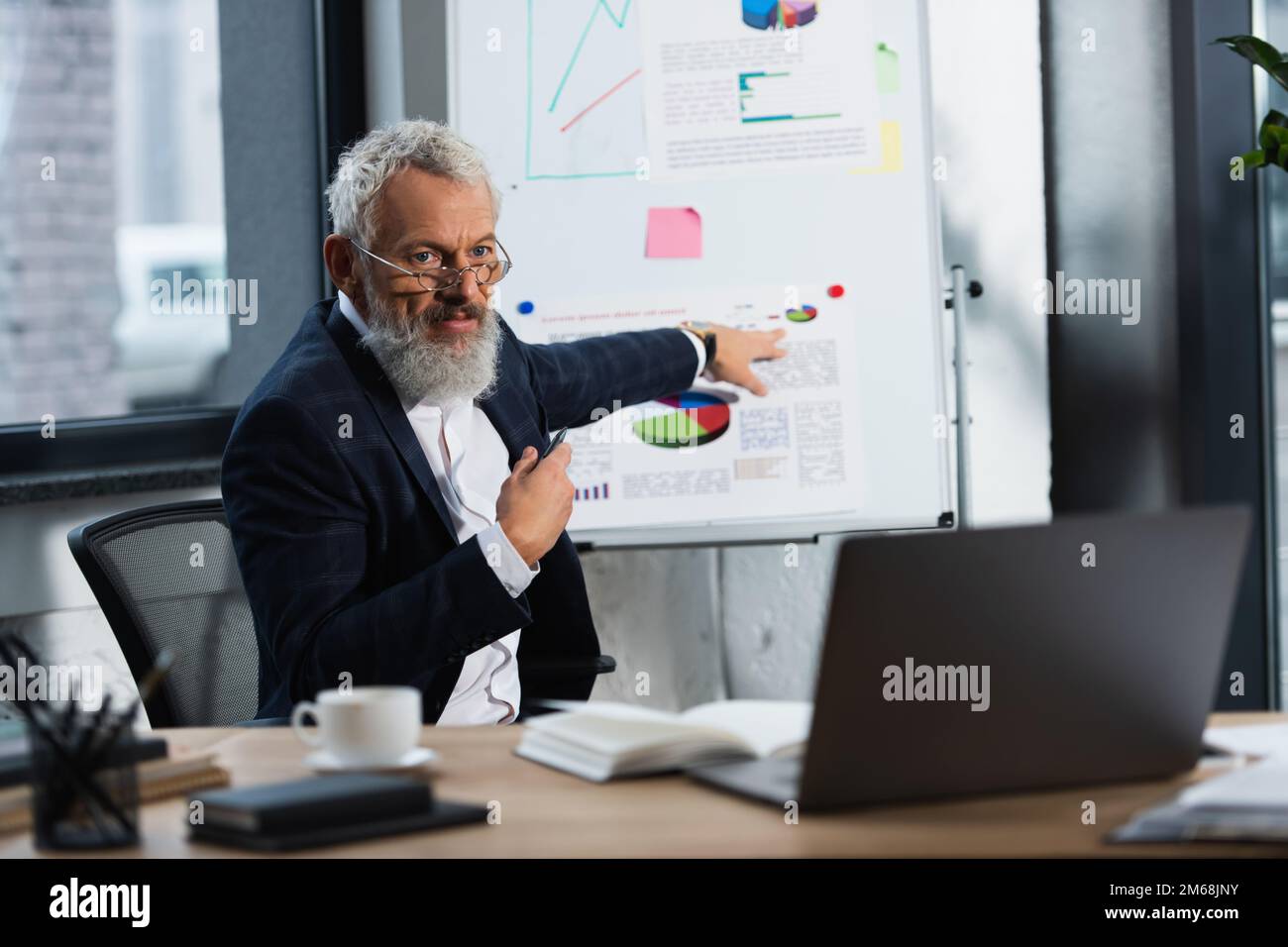 Middle aged businessman pointing at blurred flip chart during video ...