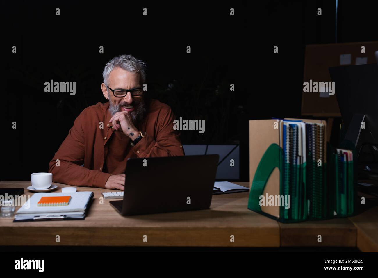 cheerful grey haired businessman looking at laptop while having video ...