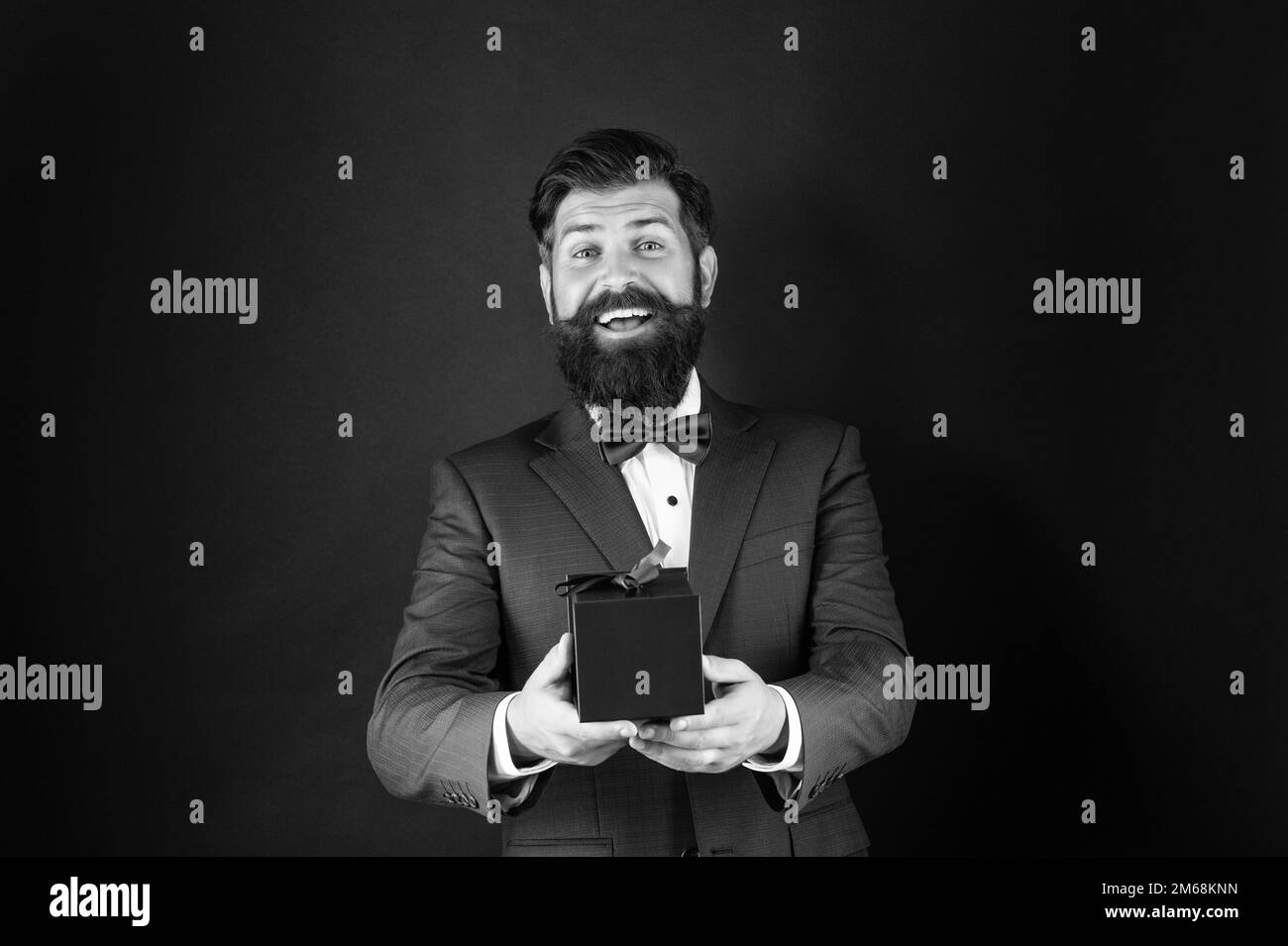 glad man in tuxedo bow tie formalwear on black background with box for ...
