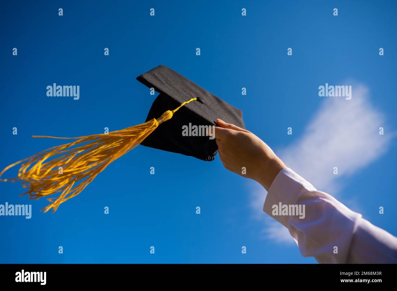 Close-up of a woman's hand with a graduation cap against the blue sky ...