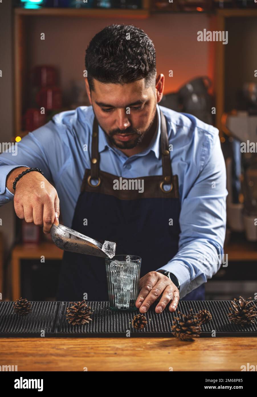 Barman holds metal scoop with ice cubes in his hand and pours them into ...