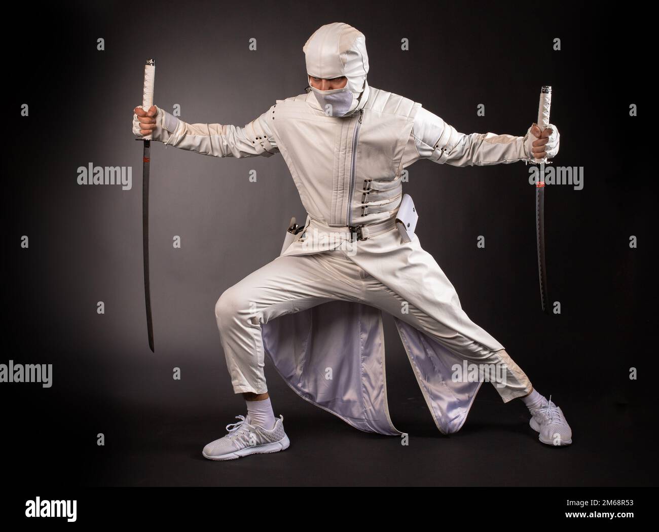 A man in the form of a combat ninja poses with two swords on a black ...