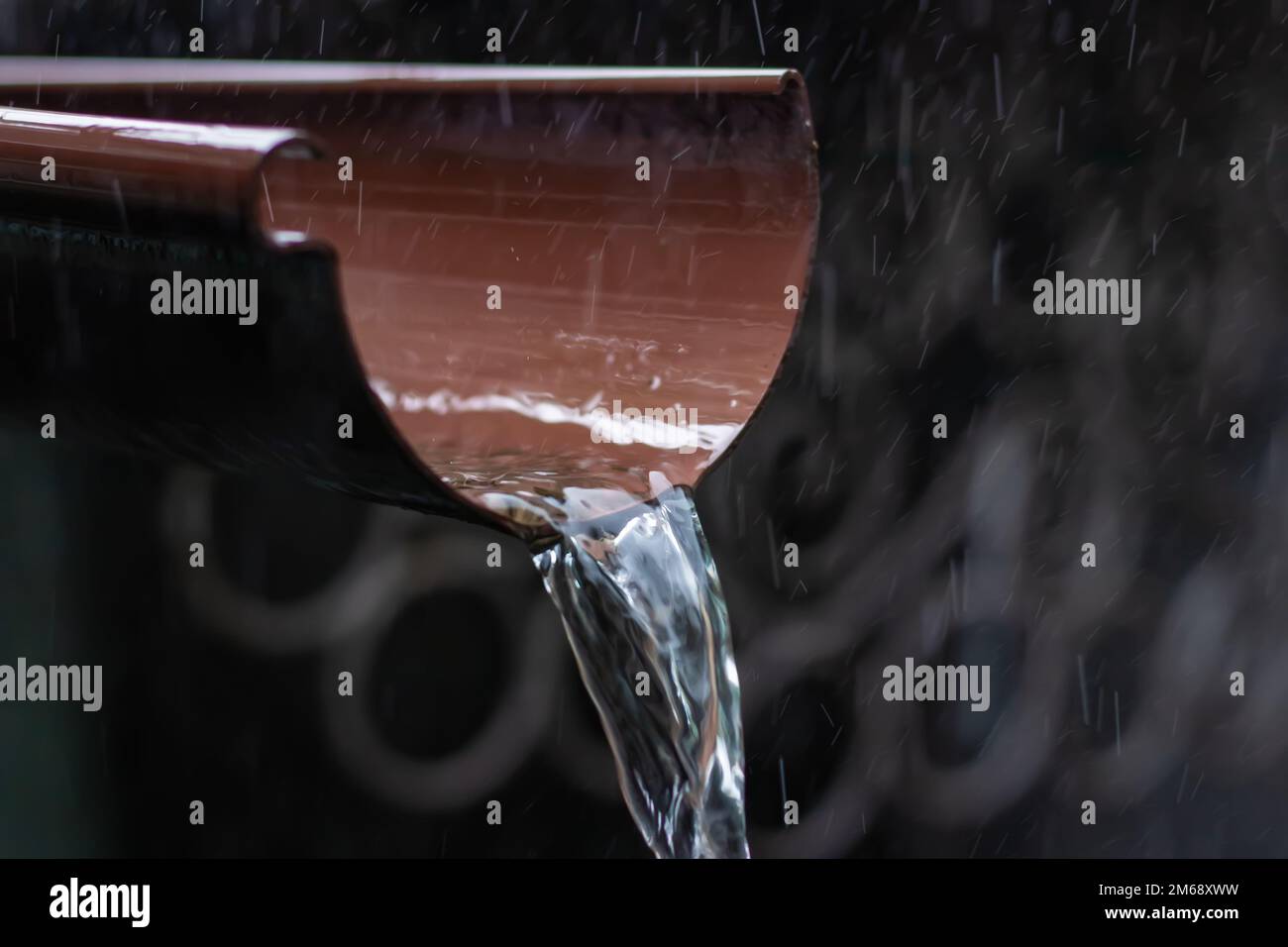 Rain water is pouring from the green draining gutter on the pavement ...