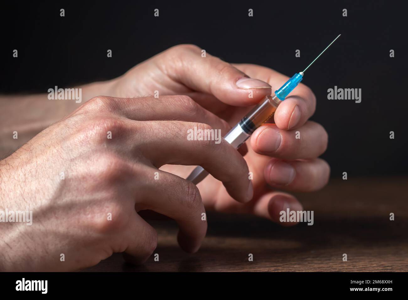 Drug syringe in hand. A drug addict with another dose of the drug in ...