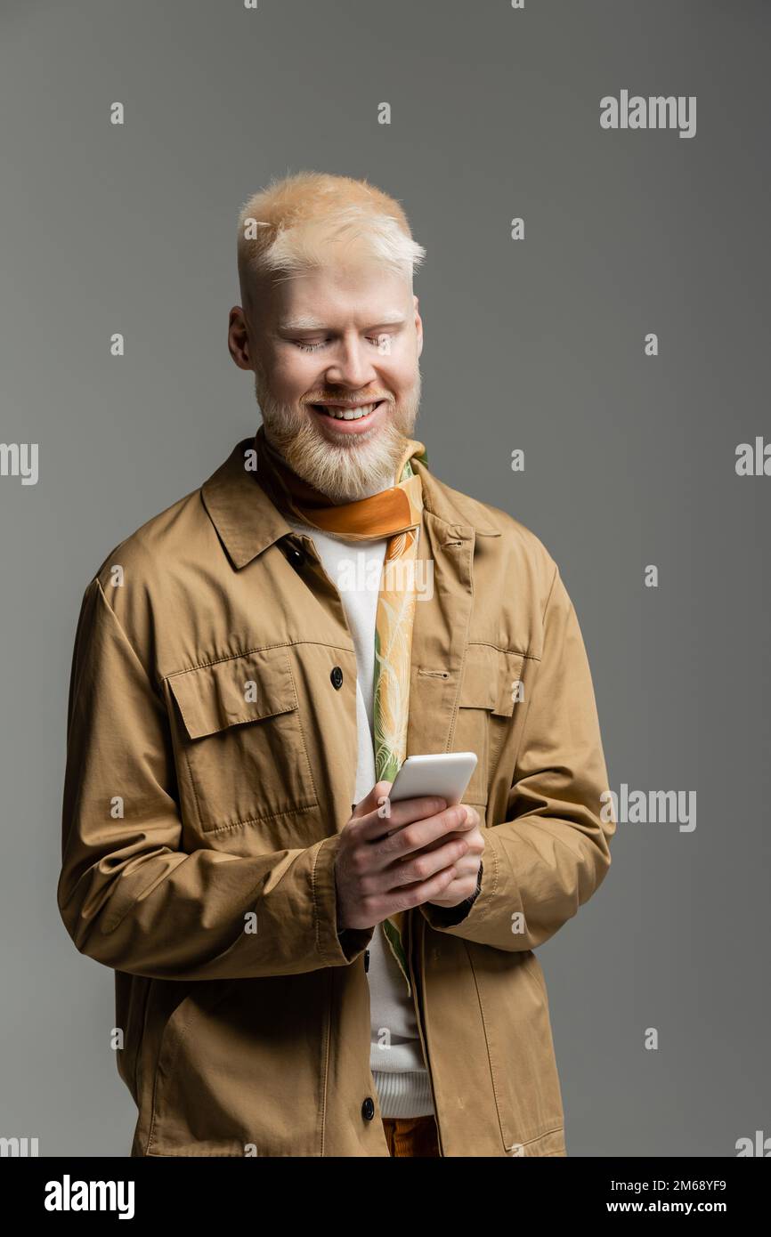 cheerful albino man in stylish shirt jacket and silk scarf messaging ...