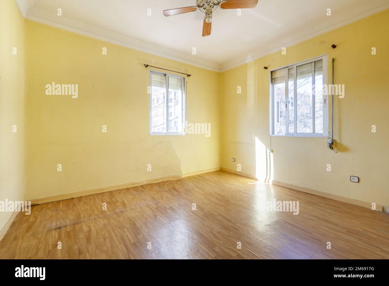 Empty living room with several windows, wooden ceiling fan and yellow ...
