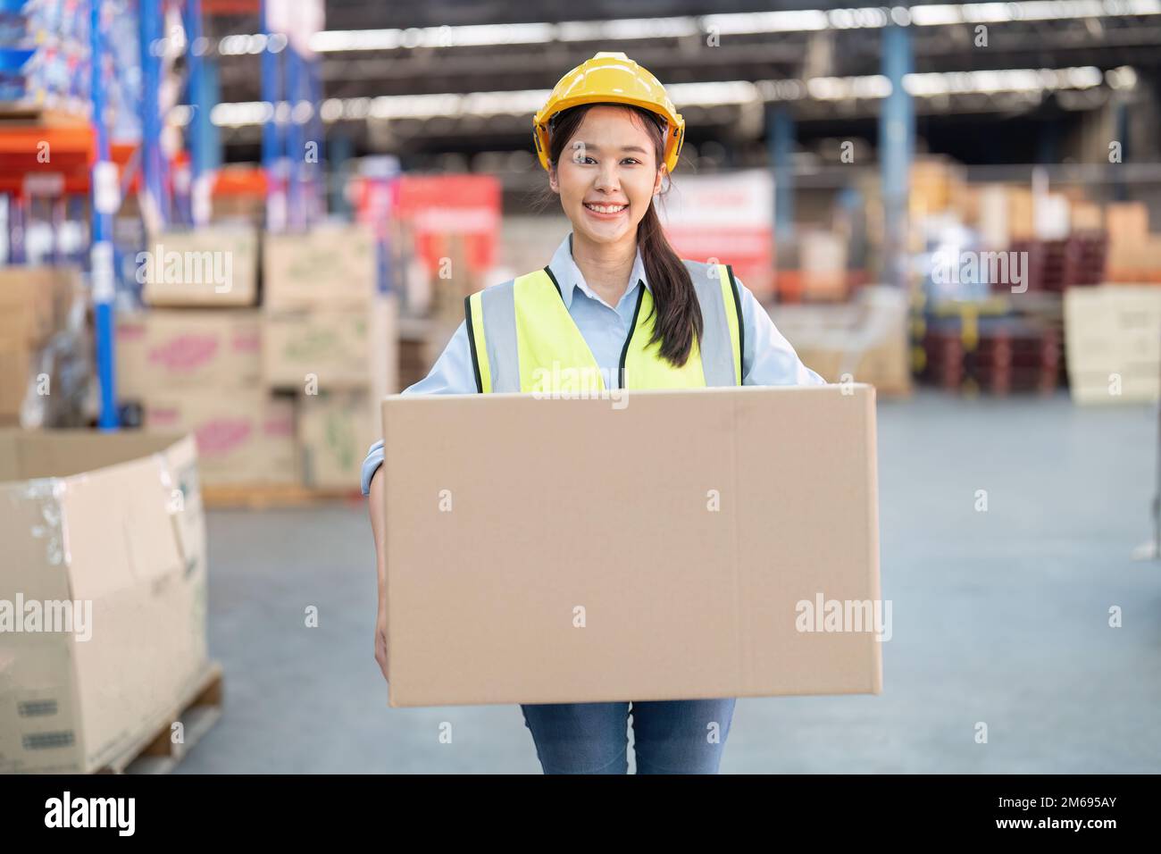 Staff working in large depot storage warehouse lift up heavy carton box ...
