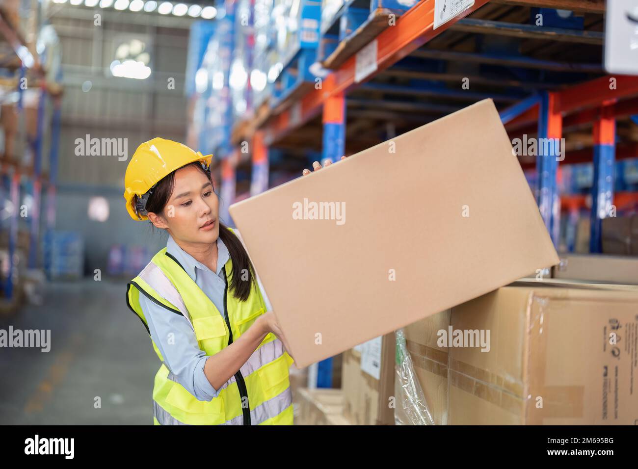 Staff working in large depot storage warehouse lift up heavy carton box ...