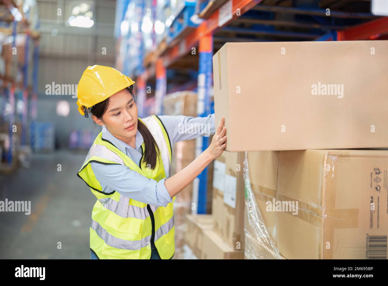 Staff working in large depot storage warehouse lift up heavy carton box ...