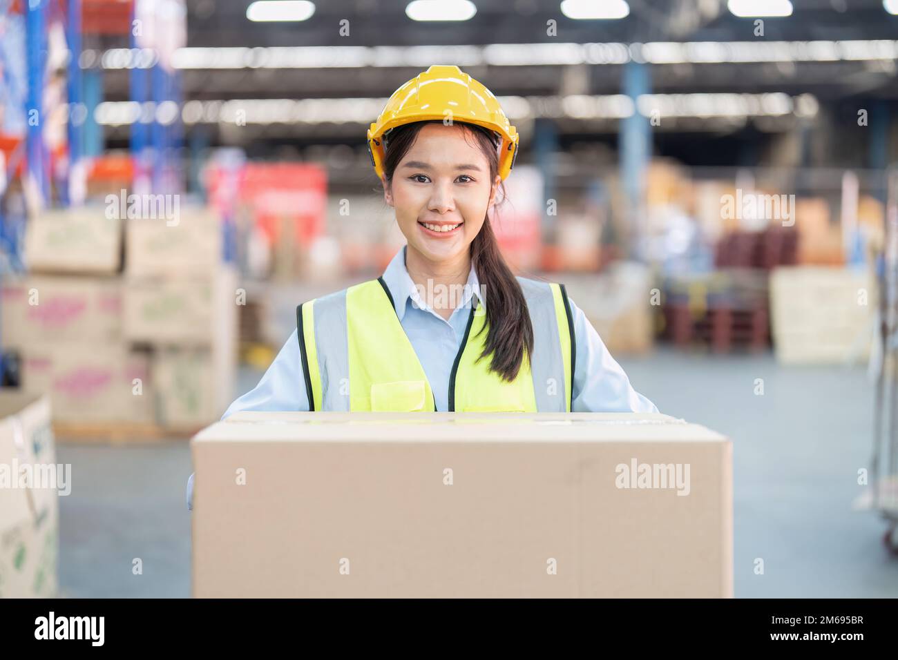 Staff working in large depot storage warehouse lift up heavy carton box ...