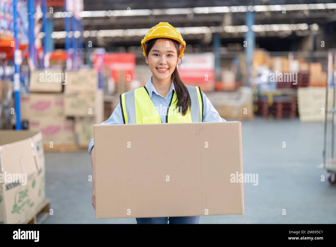 Staff working in large depot storage warehouse lift up heavy carton box ...