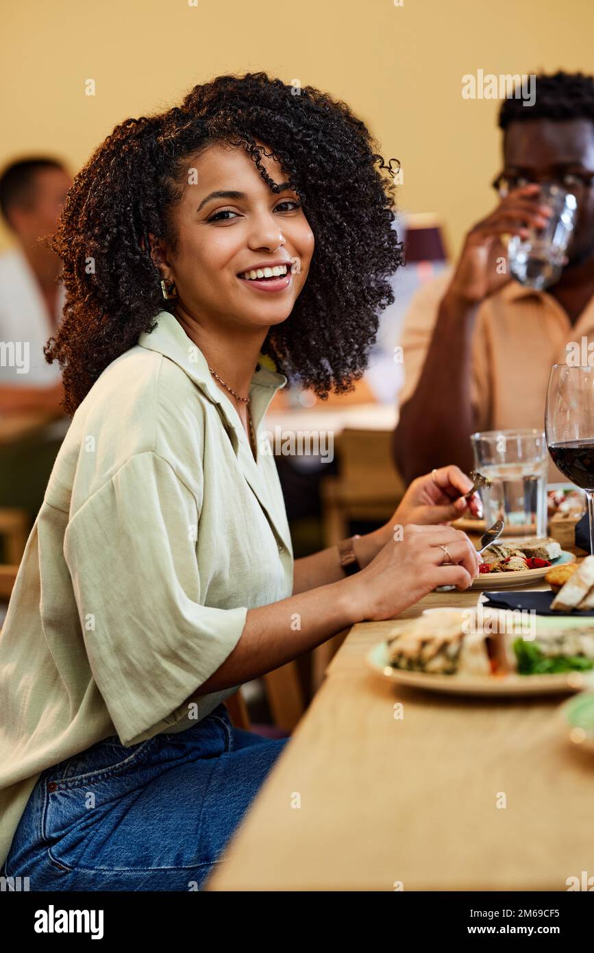 A happy hispanic girl sits in a restaurant and eating her lunch with ...