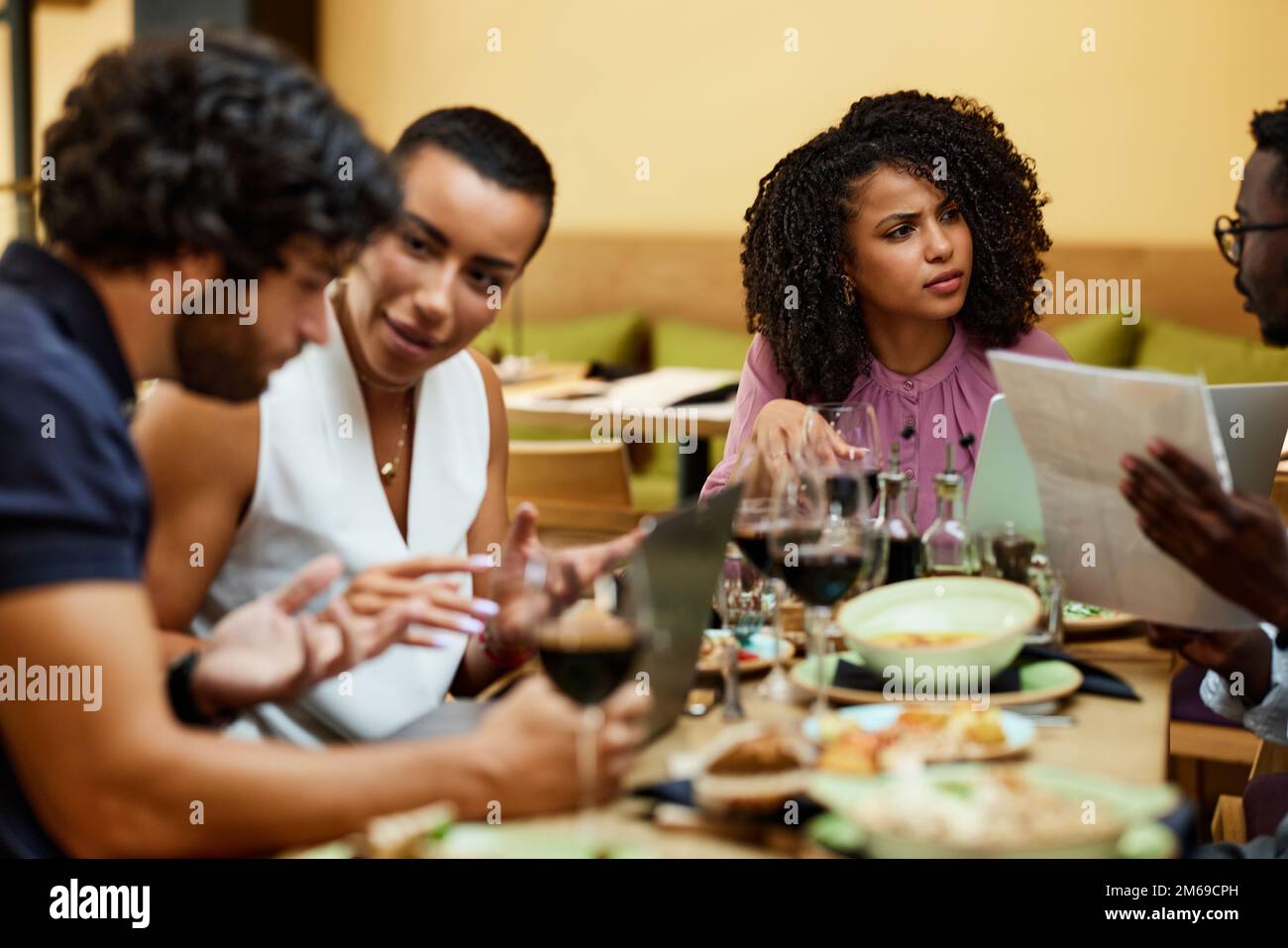 A group of multicultural managers is sitting in a restaurant at a ...