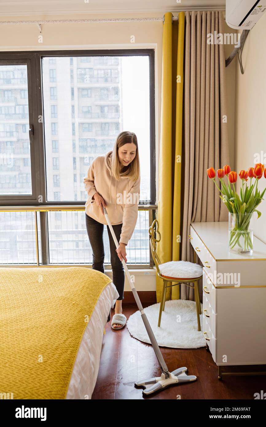 Beautiful young Caucasian blonde housewife cleaning floor in living ...