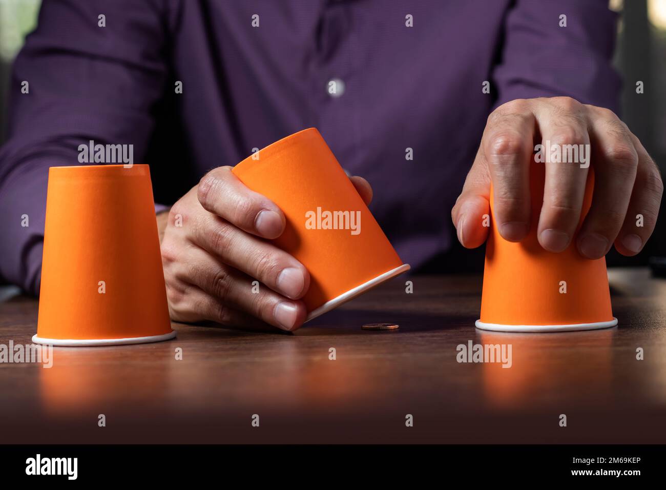 Man shows shell game of thimbles with coin, dark background. Concept ...