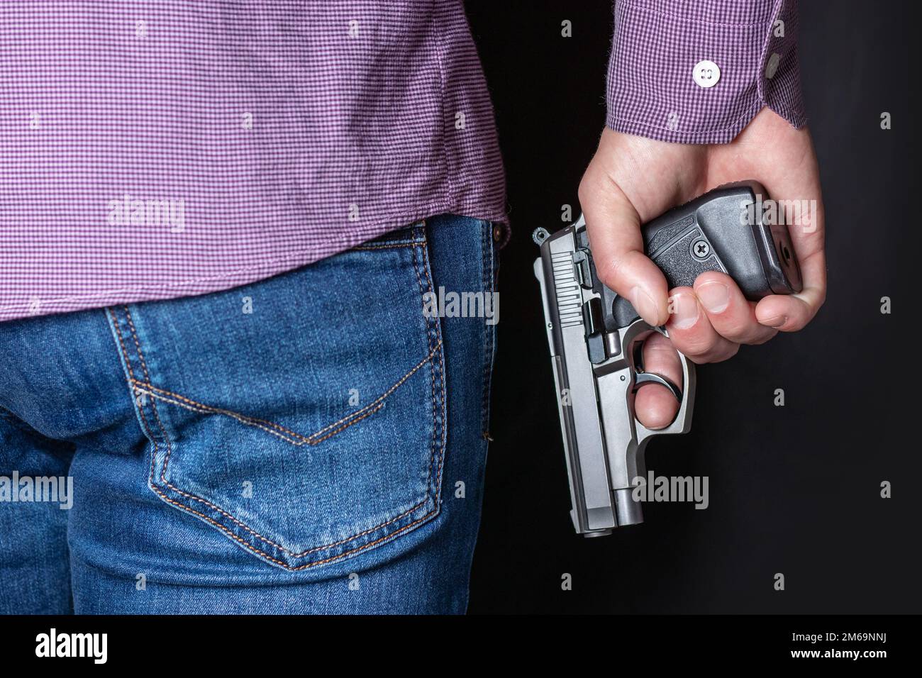 A man holding a gun in his hand behind his back, close-up view ...