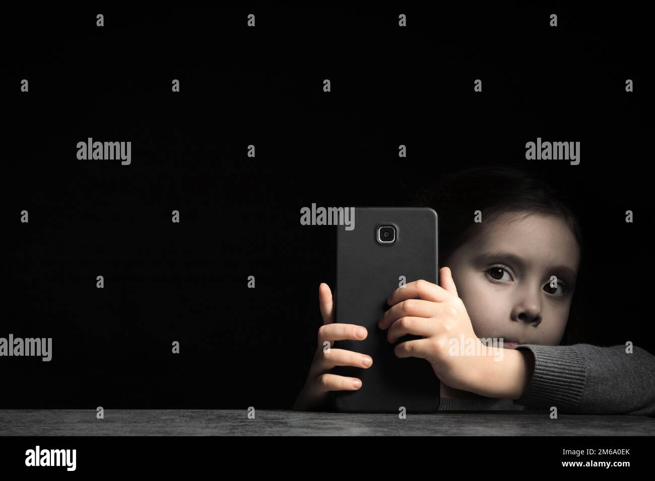 Little child with a gray face hides behind a large smartphone in his ...