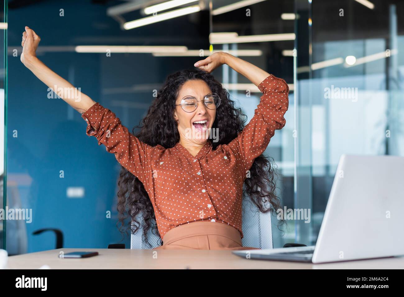 Tired businesswoman in office stretching and yawning, latin american ...