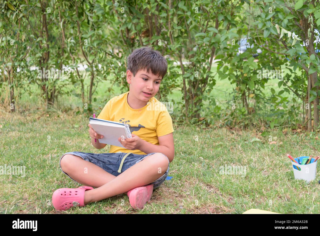 Boy sitting and relaxing on a hill reading a book in a meadow concept ...