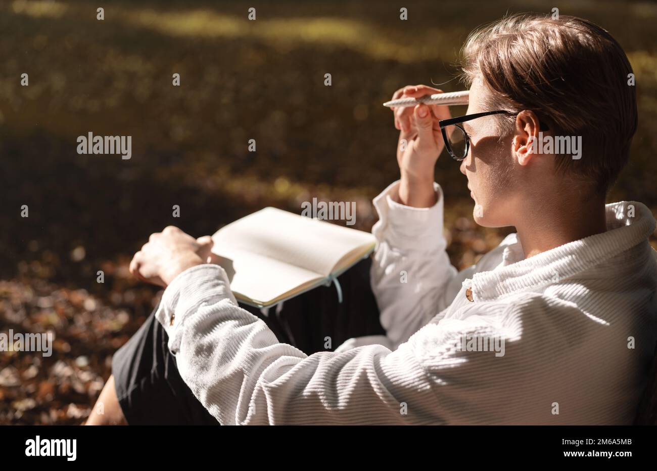 Woman sitting on ground in park with diary on hir lap and thinking ...