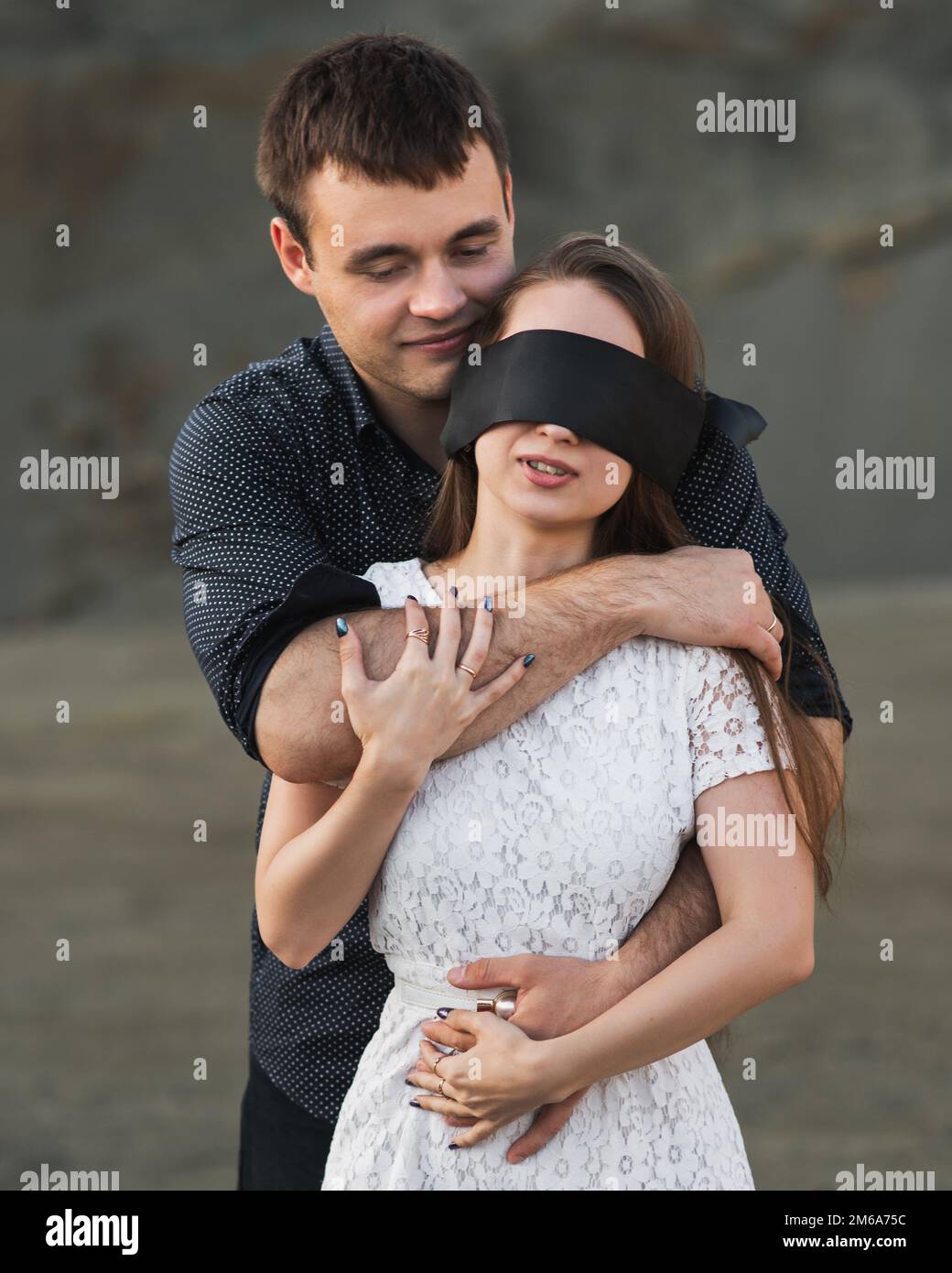 Romantic man hugging his woman blindfolded with black ribbon. Love ...