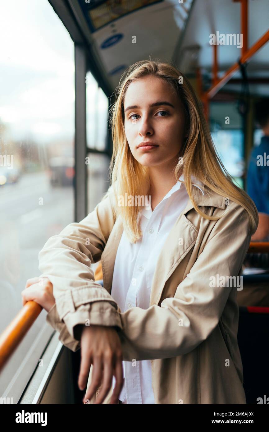 portrait of a woman in a coat and white shirt standing inside the bus ...