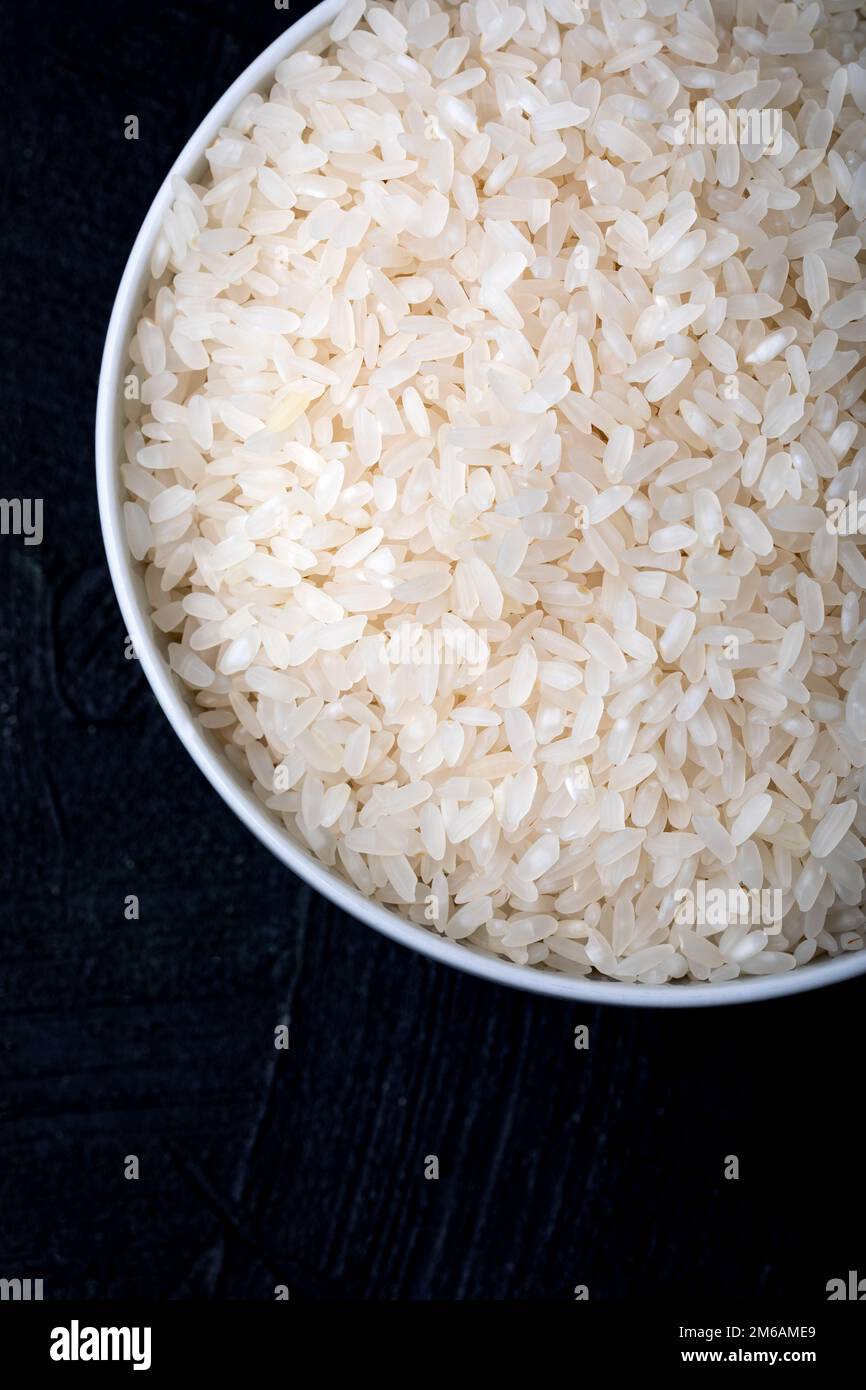 Bowl containing uncooked white rice on a black background. Top view ...