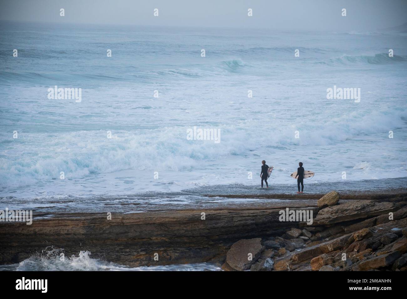 Surfer facing out to sea while wave crashes in front of him Stock Photo ...