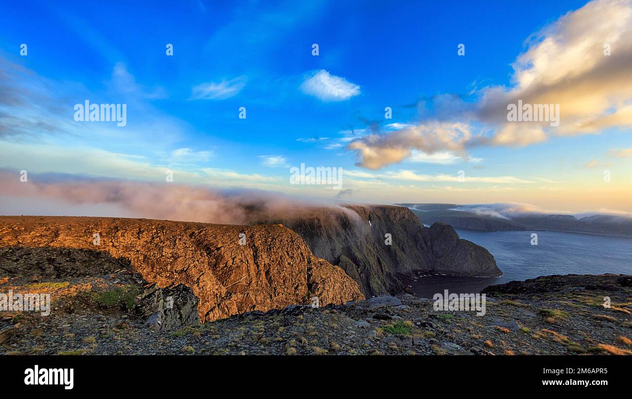 Rocky shale coast, clouds illuminated by the midnight sun at North Cape ...