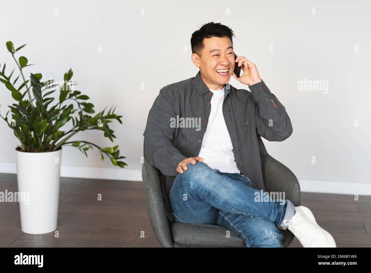 Cheerful middle aged asian man calling by phone, sitting in armchair in ...