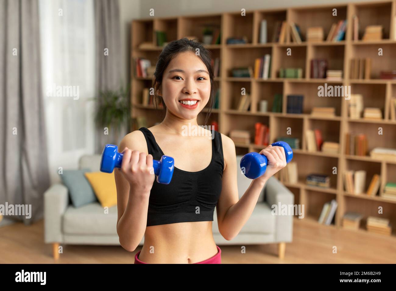 Cheerful asian lady doing dumbbell workout at home, working on arms ...